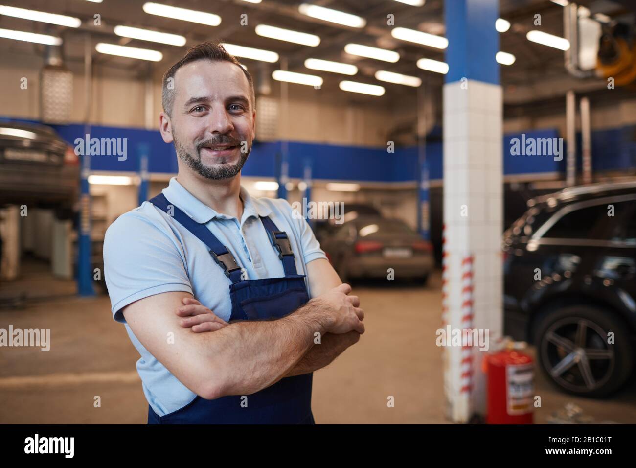 Waist up portrait of smiling car mechanic standing with arms crossed ...