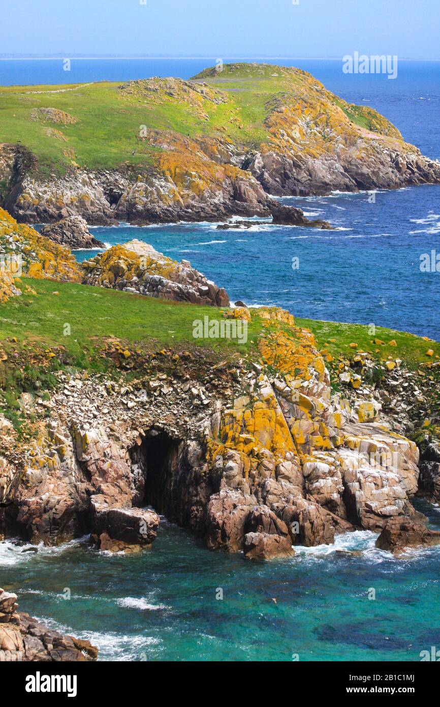 Irish coastal landscape. Sea arch, green grass and yellow lichen rocky ...