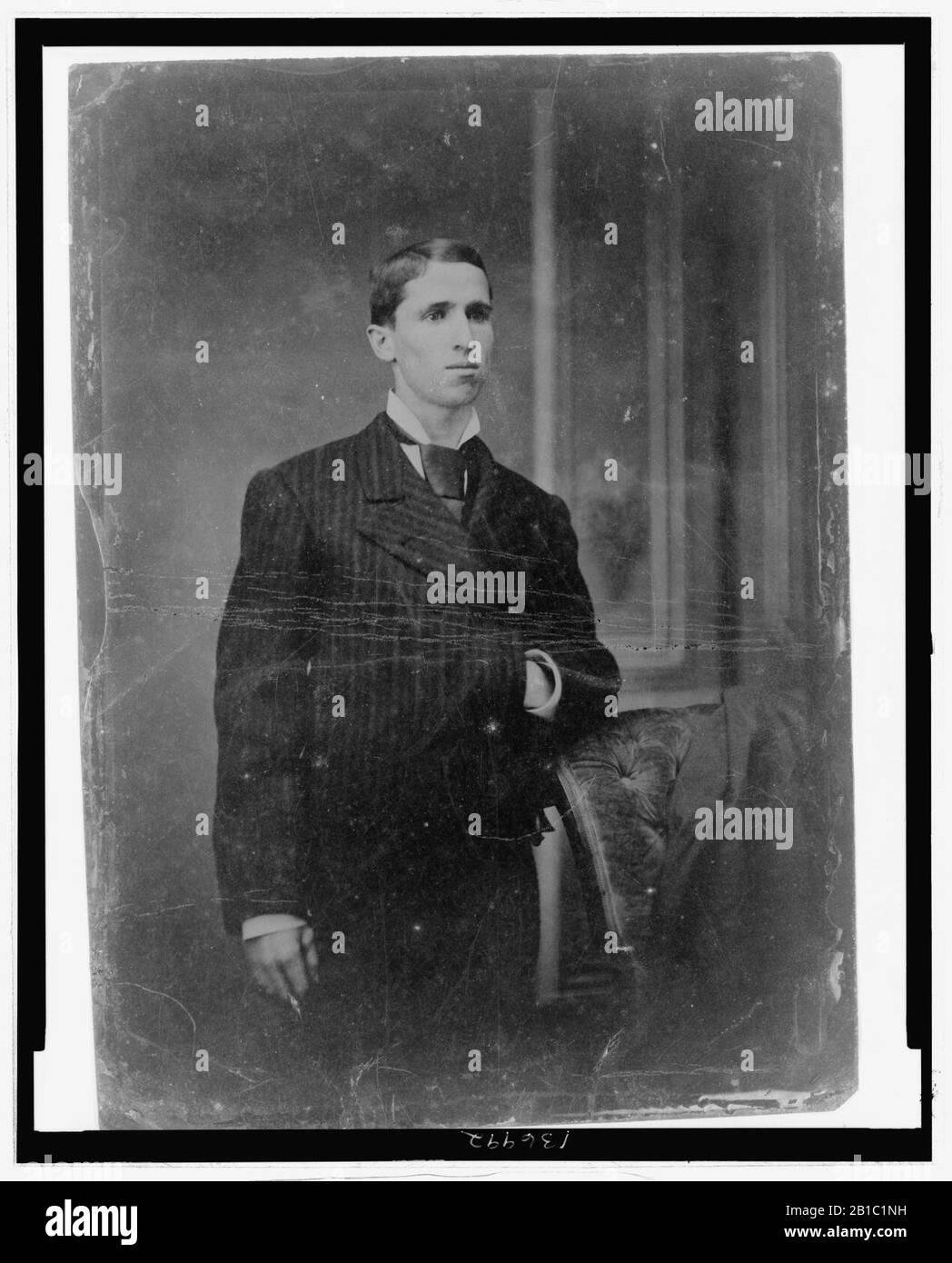 Full-length portrait of a young man, standing with one hand in suit ...