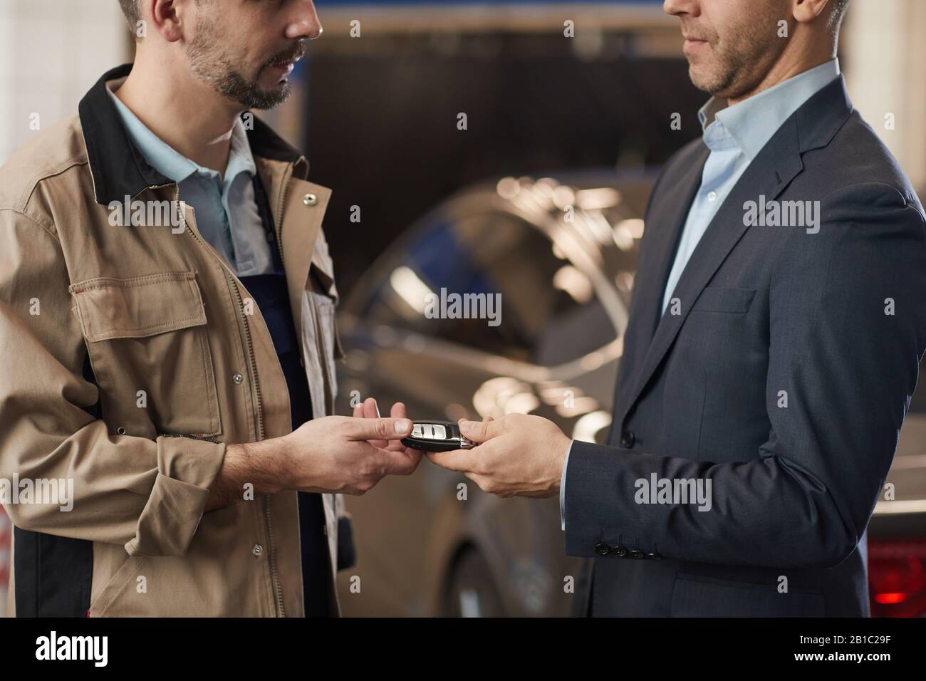 Mid section of mechanic giving car keys to businessman after checking ...