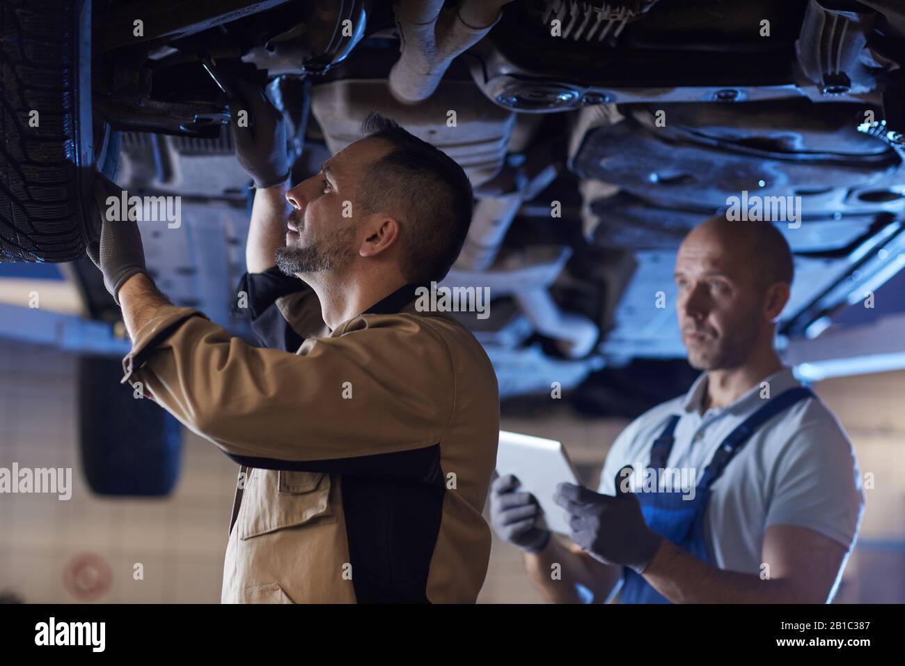 Portrait of two mechanics standing under car on lift while inspecting ...