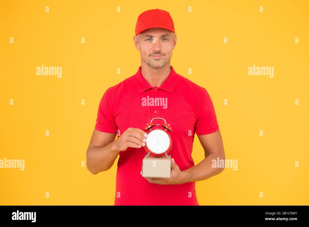 On time delivery. Delivery man yellow background. Courier hold clock ...