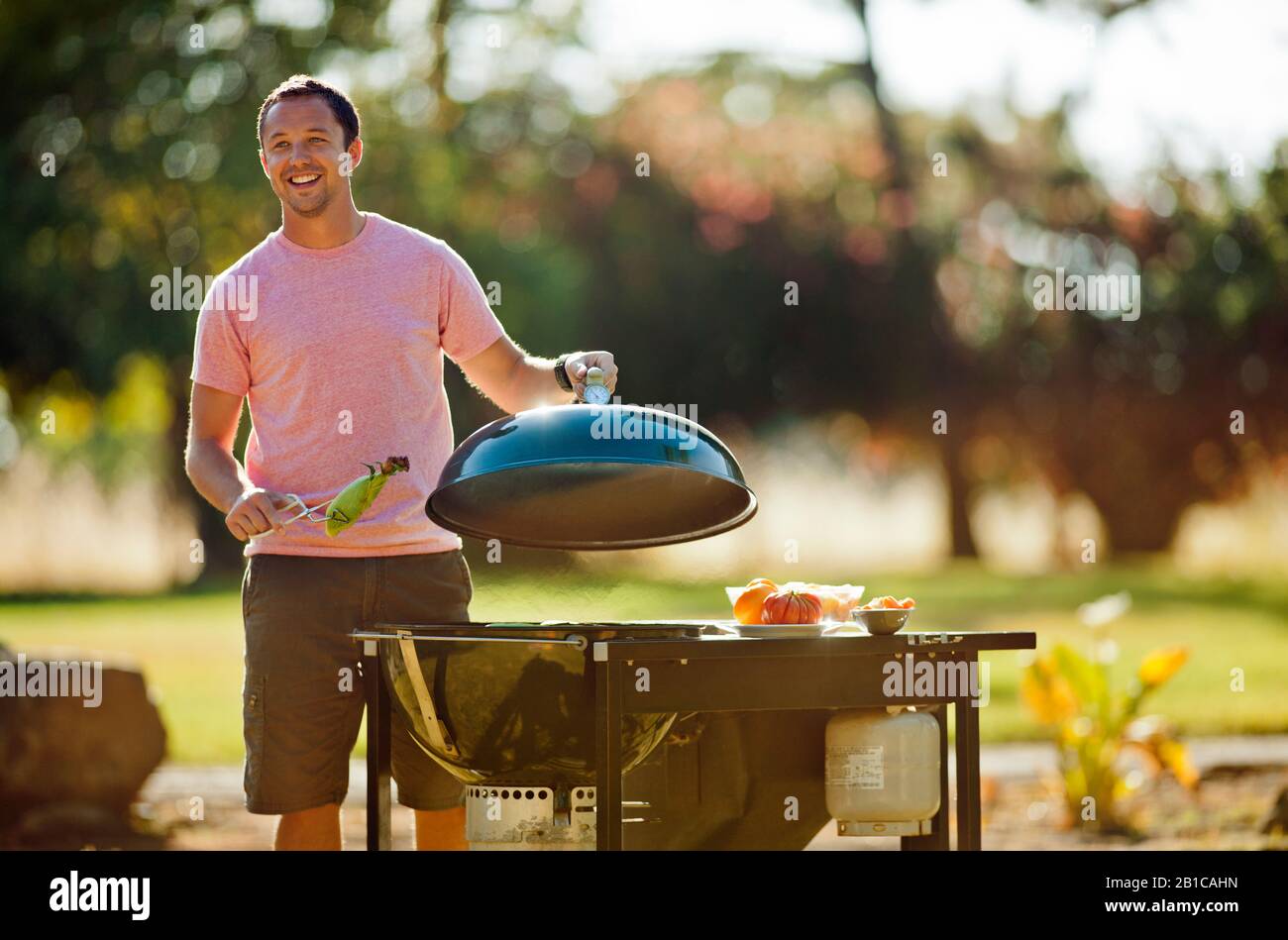 Smiling man standing next to a barbecue Stock Photo - Alamy