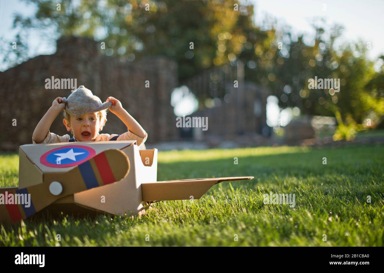 Happy young boy playing with a home made cardboard plane in the back ...