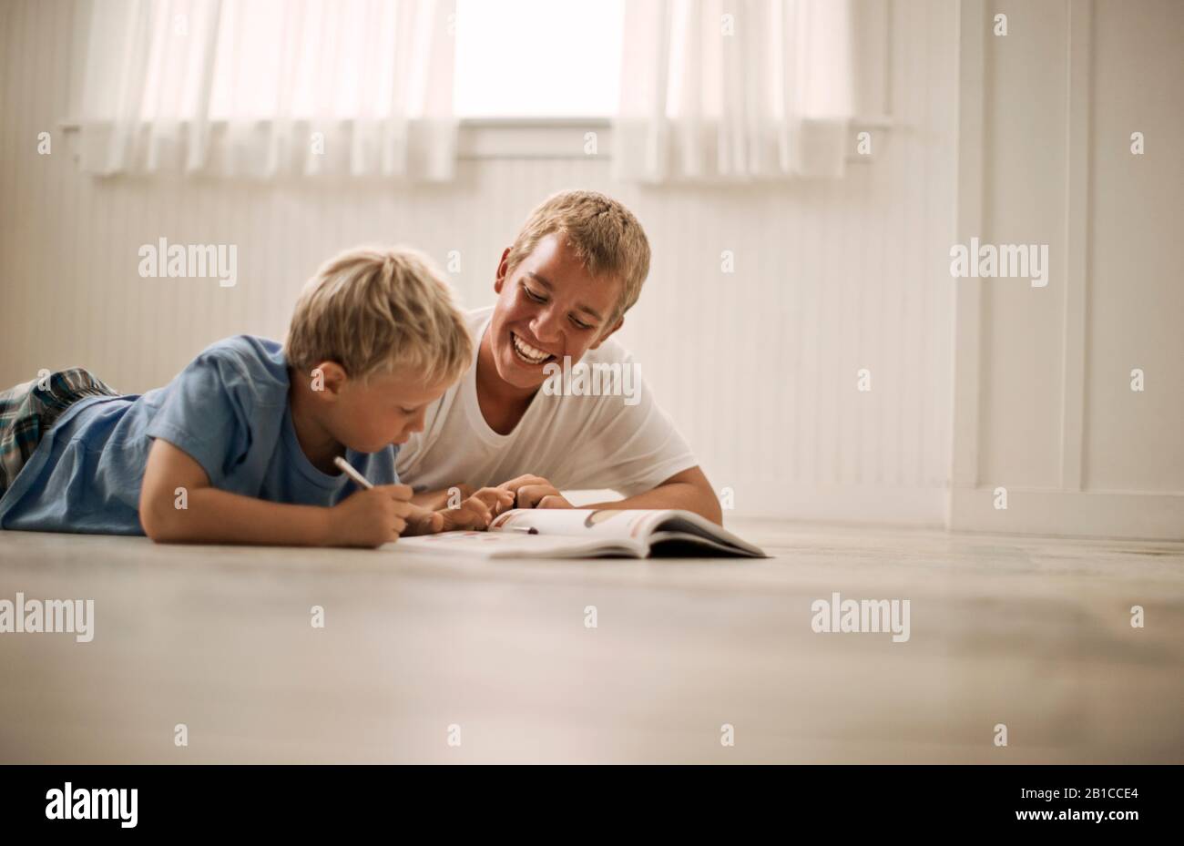 Teenage boy lying on the floor helping his younger brother with ...