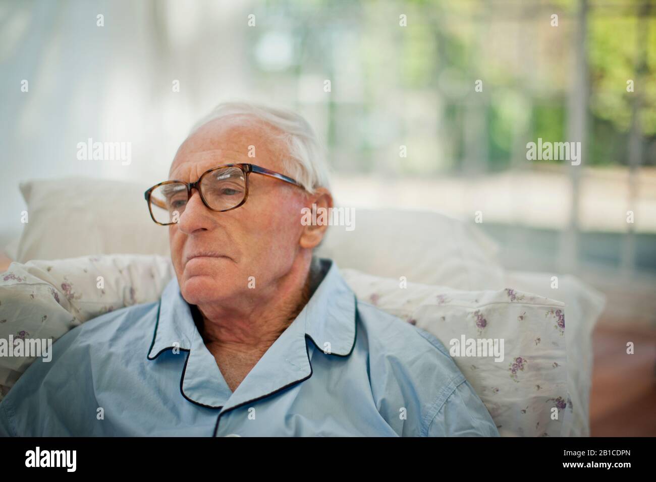 Worried senior man lying in bed in a rest home Stock Photo - Alamy