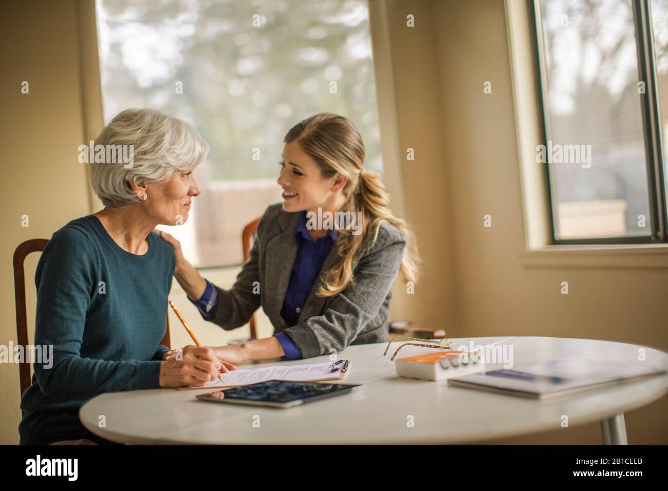 Mid adult woman encouraging a senior woman to sign a document at a ...