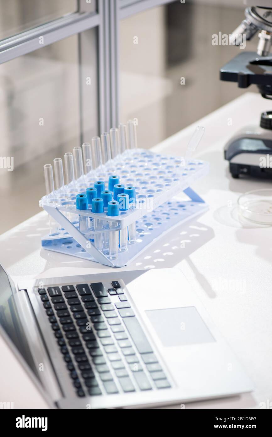 Close-up of workplace with open laptop, test tube rack and microscope ...