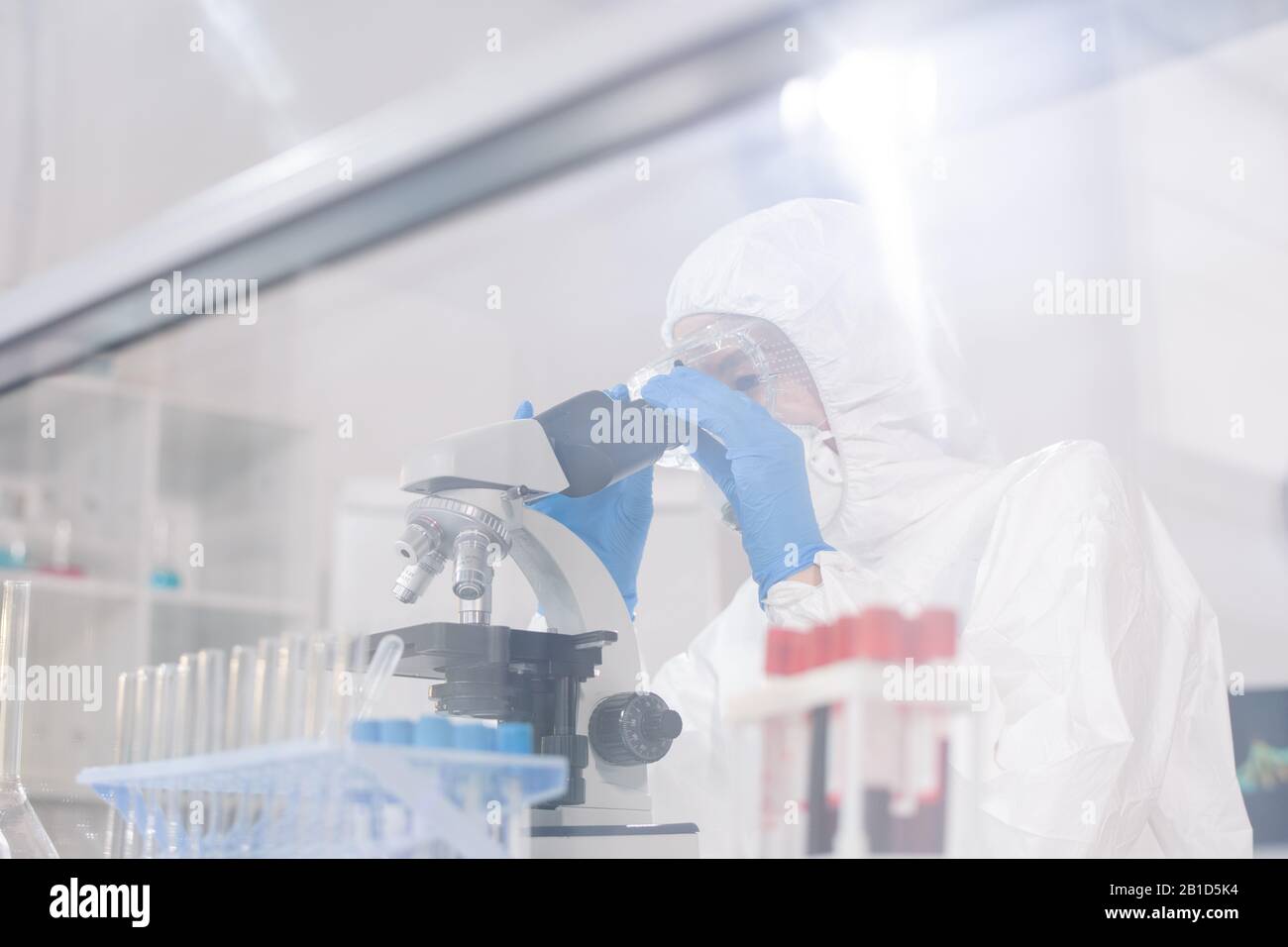 Behind glass view of virology scientist in protective suit analyzing ...