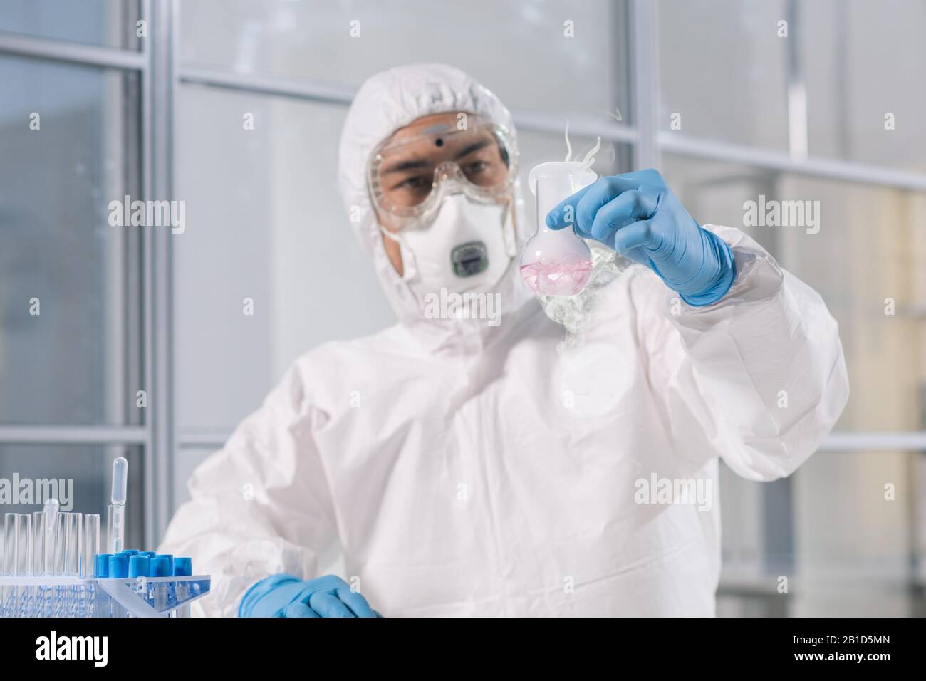 Busy scientific researcher in mask holding flask of smoking reagent ...