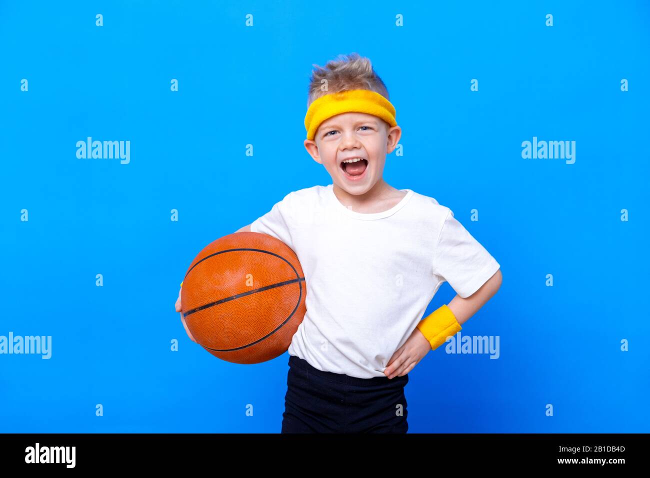 Sporty little boy with basketball ball over blue studio background. Gym ...