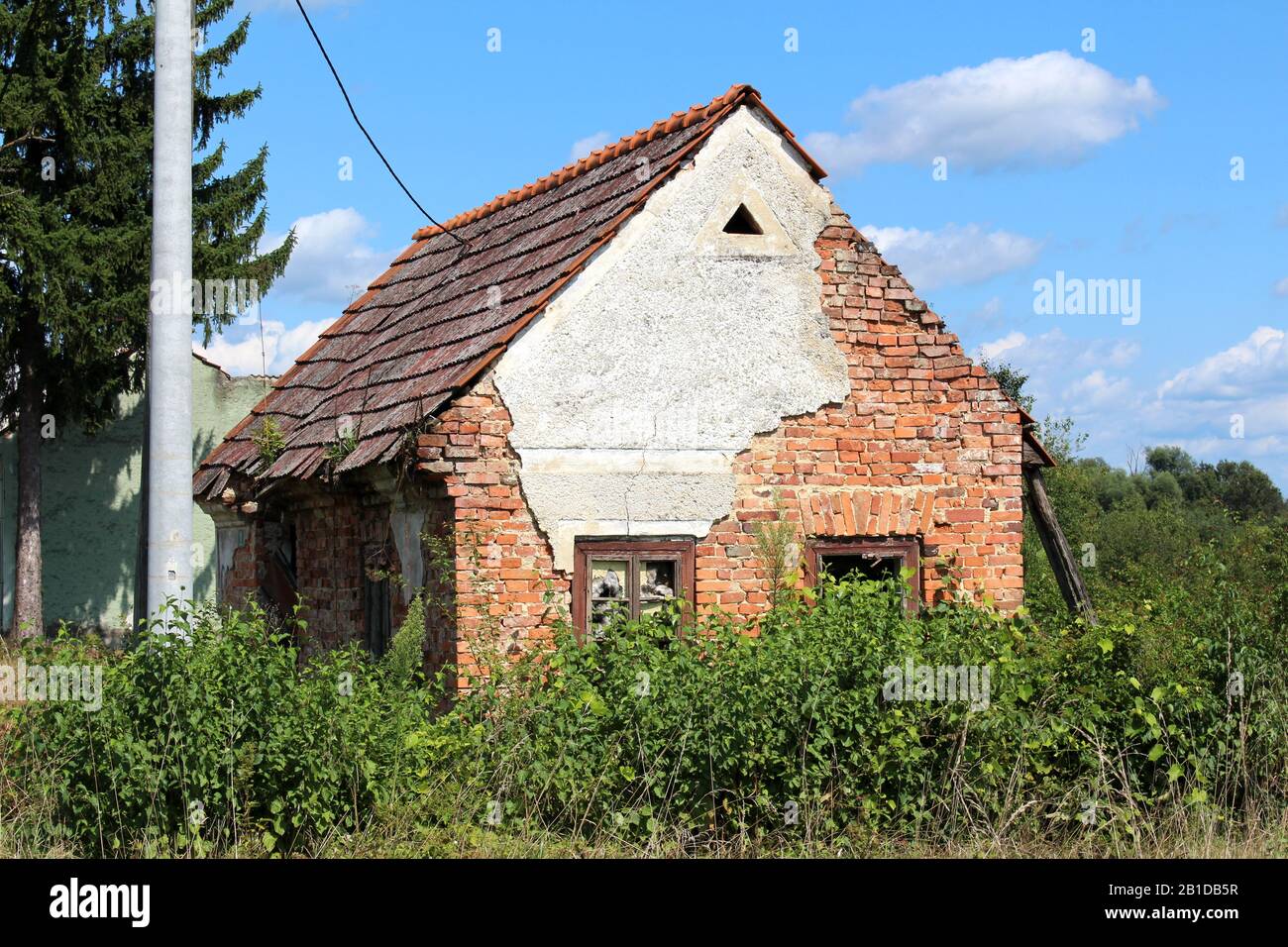 Abandoned small red bricks suburban family house ruins with broken windows and destroyed roof ...