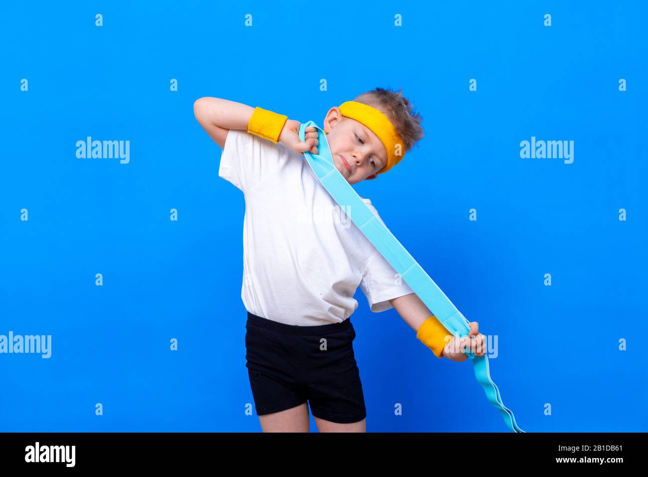 Sporty little boy with rubber fitness band over blue studio background ...
