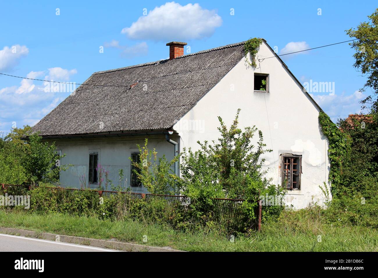 Abandoned small white suburban family house with broken windows and dilapidated facade covered ...