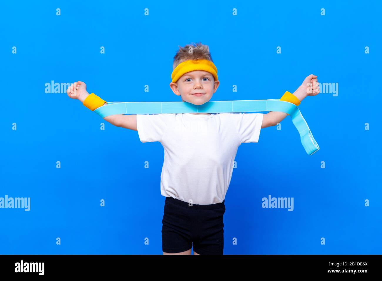 Sporty little boy with rubber fitness band over blue studio background ...