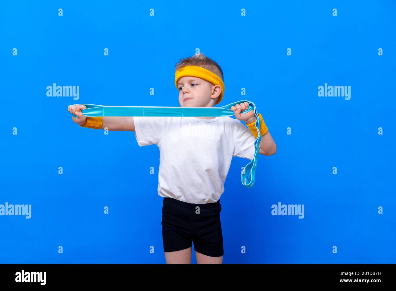 Sporty little boy with rubber fitness band over blue studio background ...