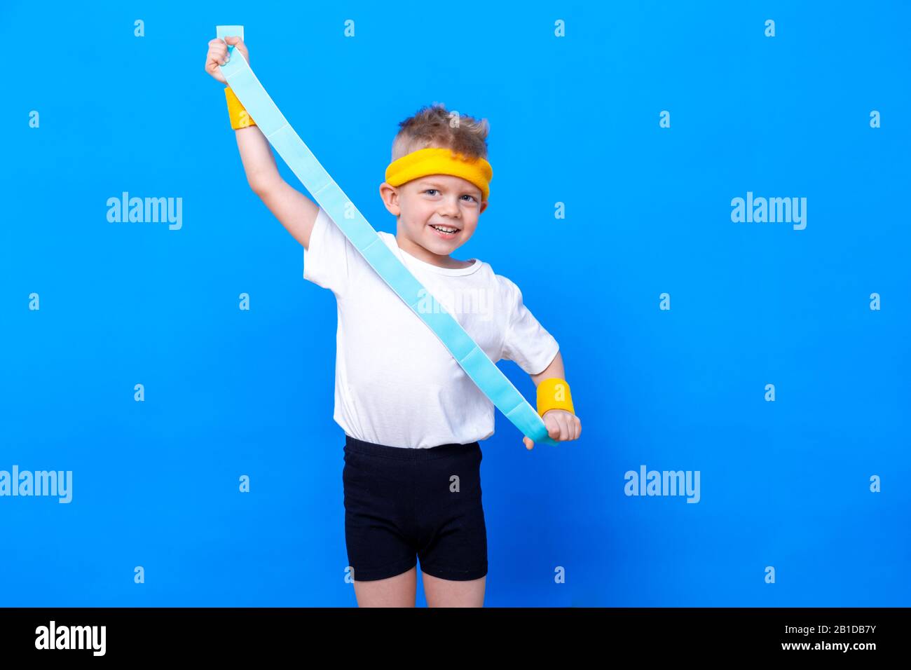 Sporty little boy with rubber fitness band over blue studio background ...