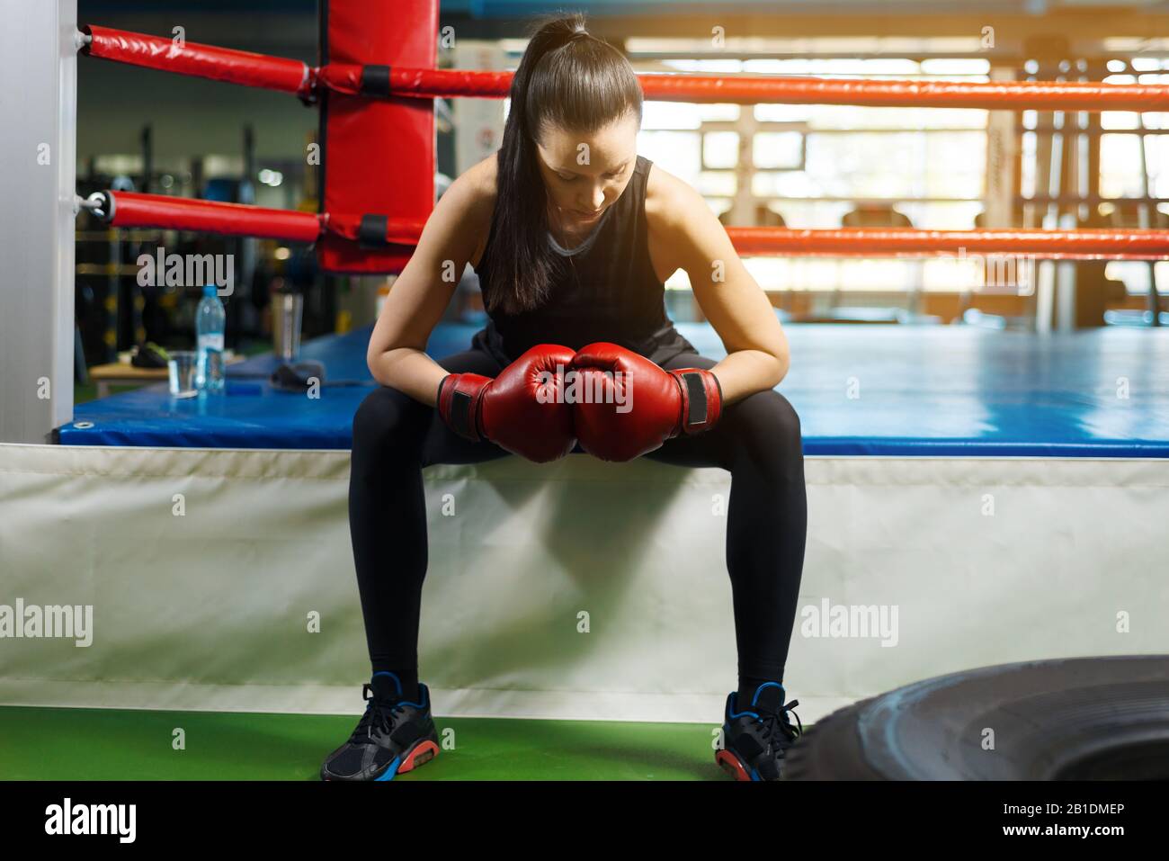 tired girl athlete sitting in the boxing ring. beautiful woman holds ...