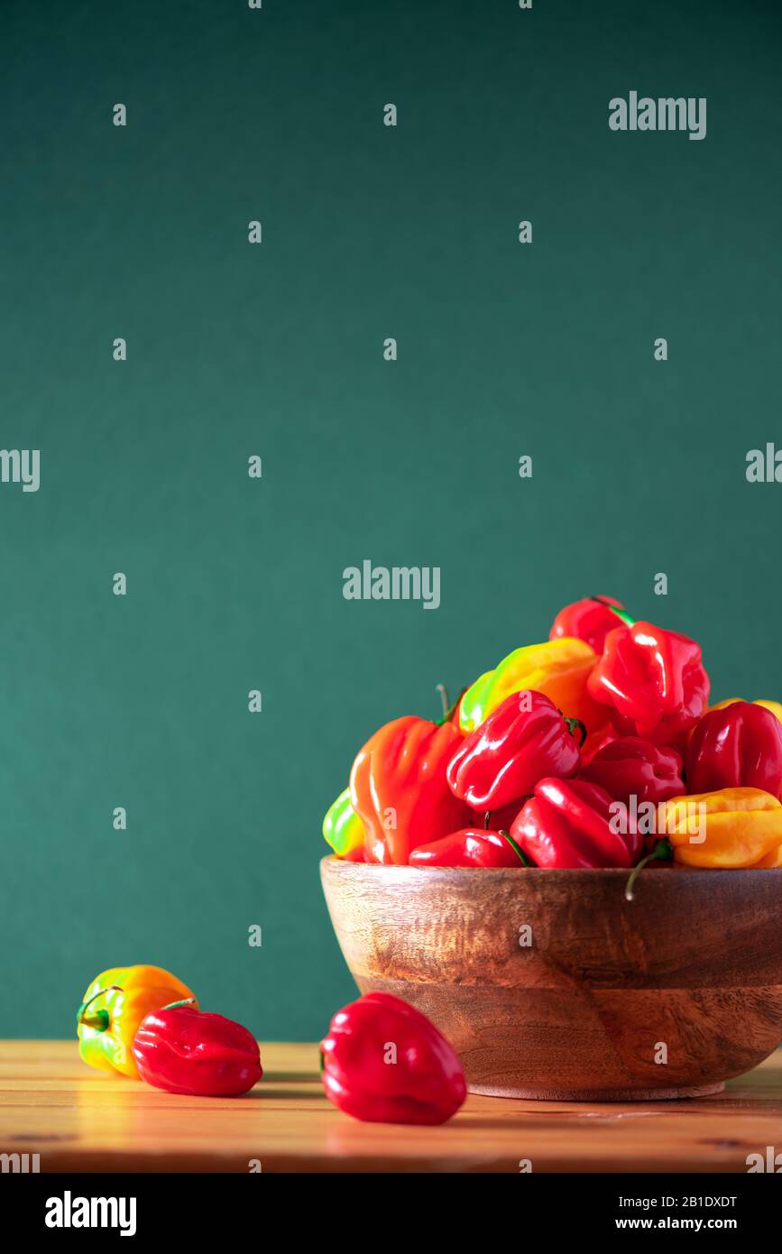 Colorful scotch bonnet chili peppers in wooden bowl over green ...