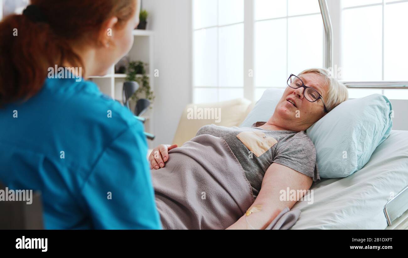 In nursing home old sick lady lying in hospital bed talks with a female ...