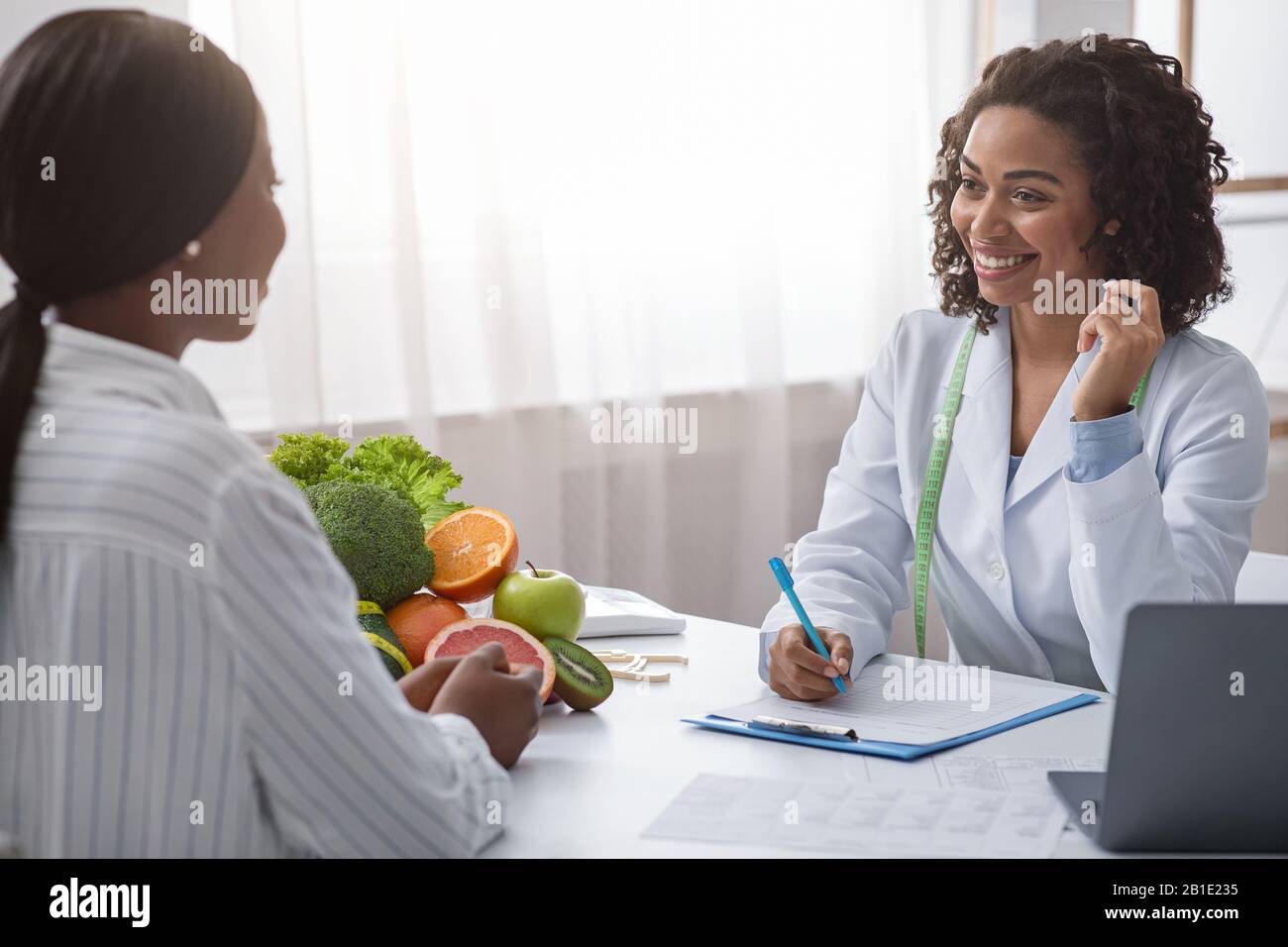 Smiling black woman talking to female patient, taking notes Stock Photo ...