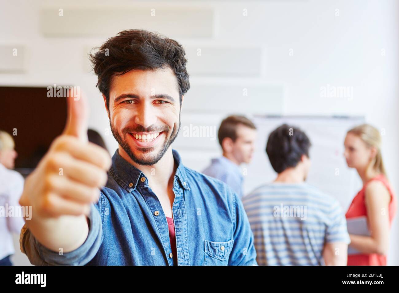 Smiling student in a start-up company holds his thumb up Stock Photo ...
