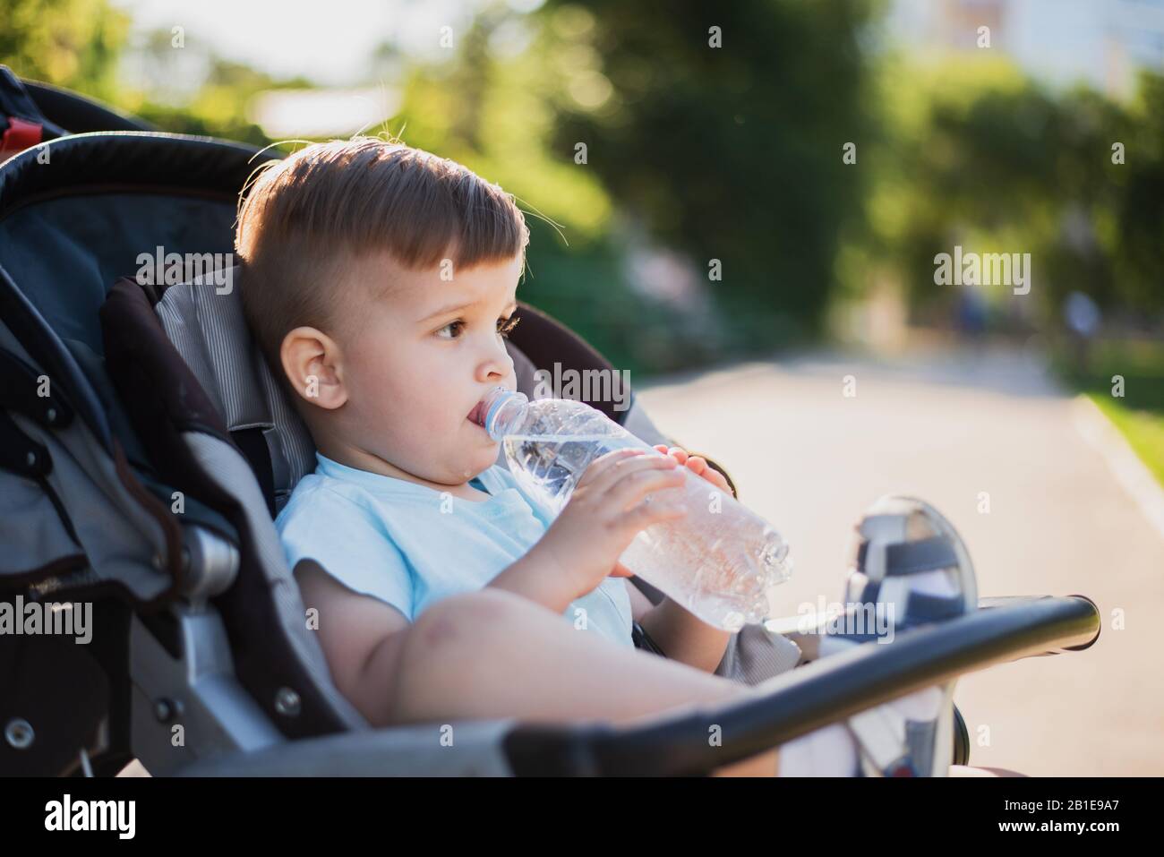 cute baby sits in a stroller and drinks clean water and on a hot summer ...