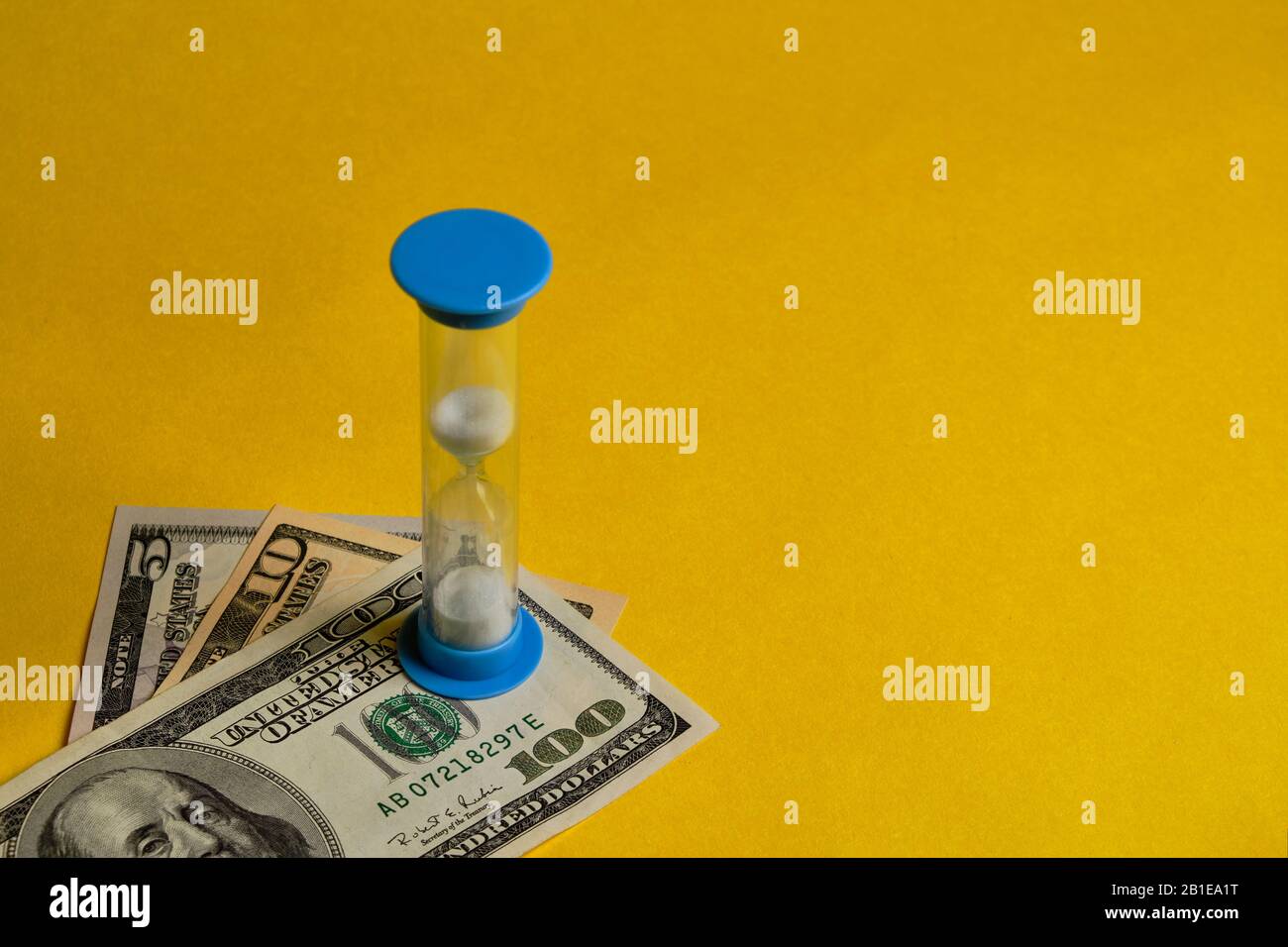 Blue hourglass and dollars at yellow background. Time management ...