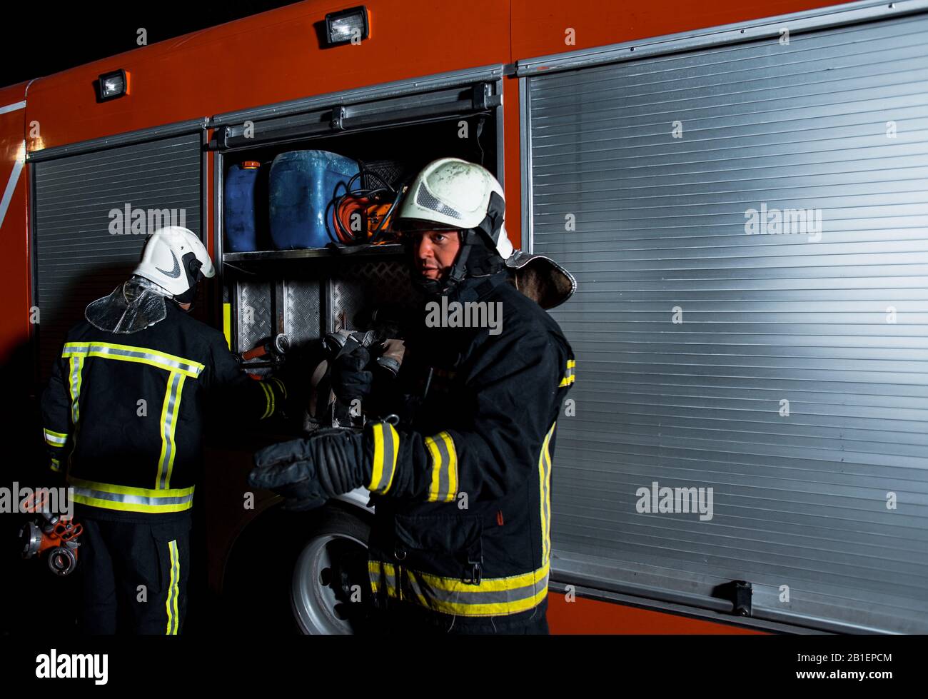 Fire service team in uniform with protective helmets extinguishing a ...