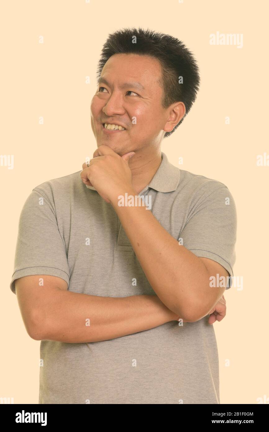 Studio shot of happy Japanese man smiling while thinking Stock Photo ...