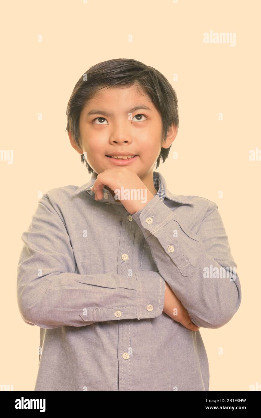 Studio shot of happy cute Japanese boy smiling and thinking while ...