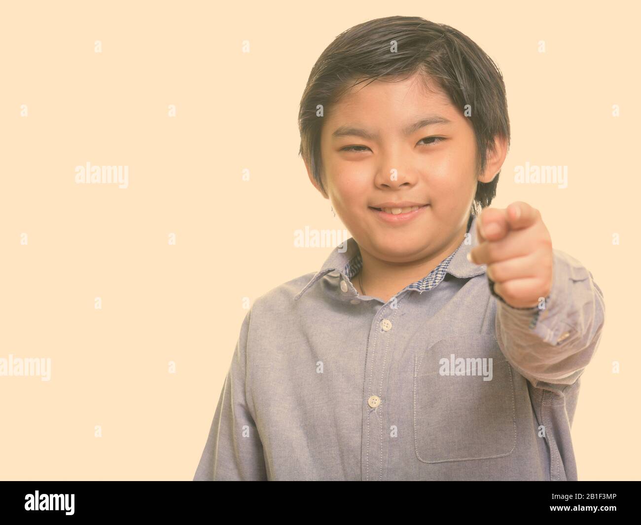 Studio shot of happy cute Japanese boy smiling while pointing finger at ...