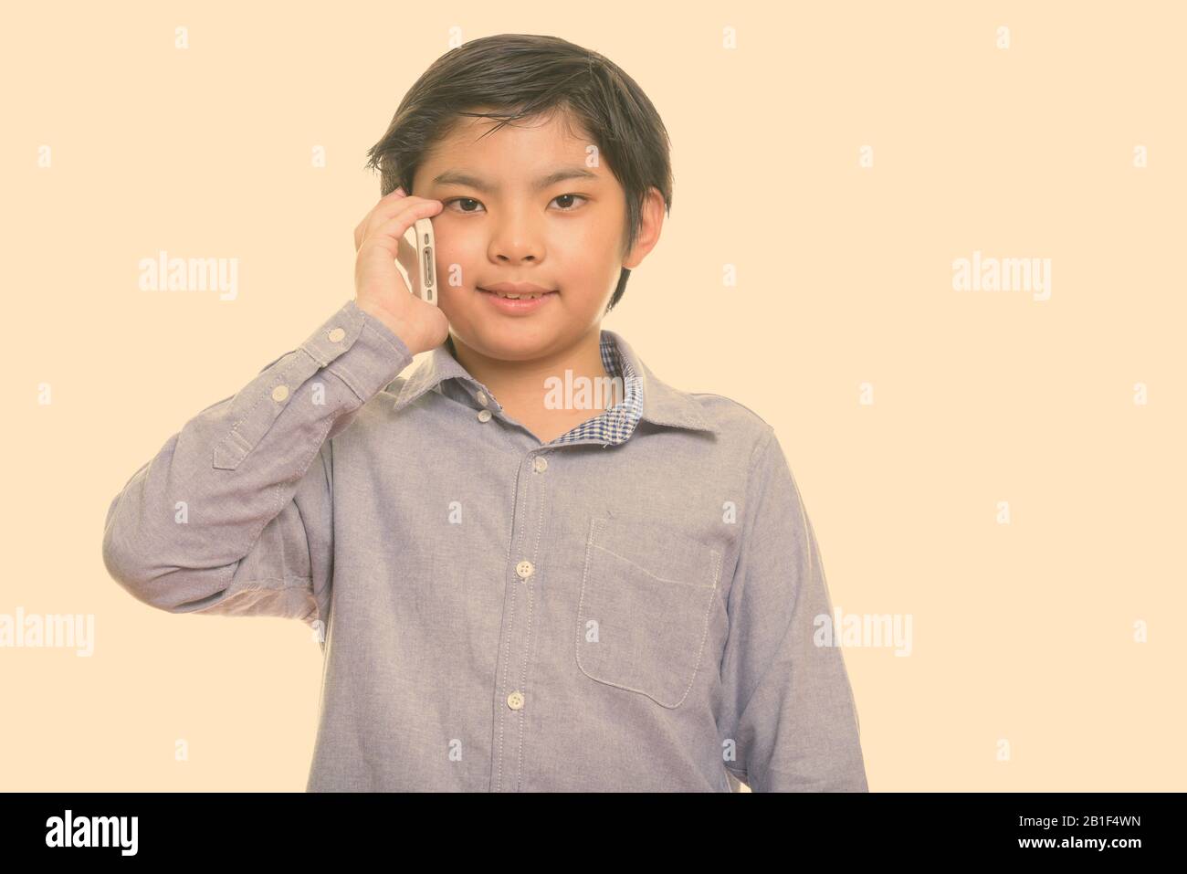 Studio shot of happy Japanese boy smiling while talking on mobile phone ...
