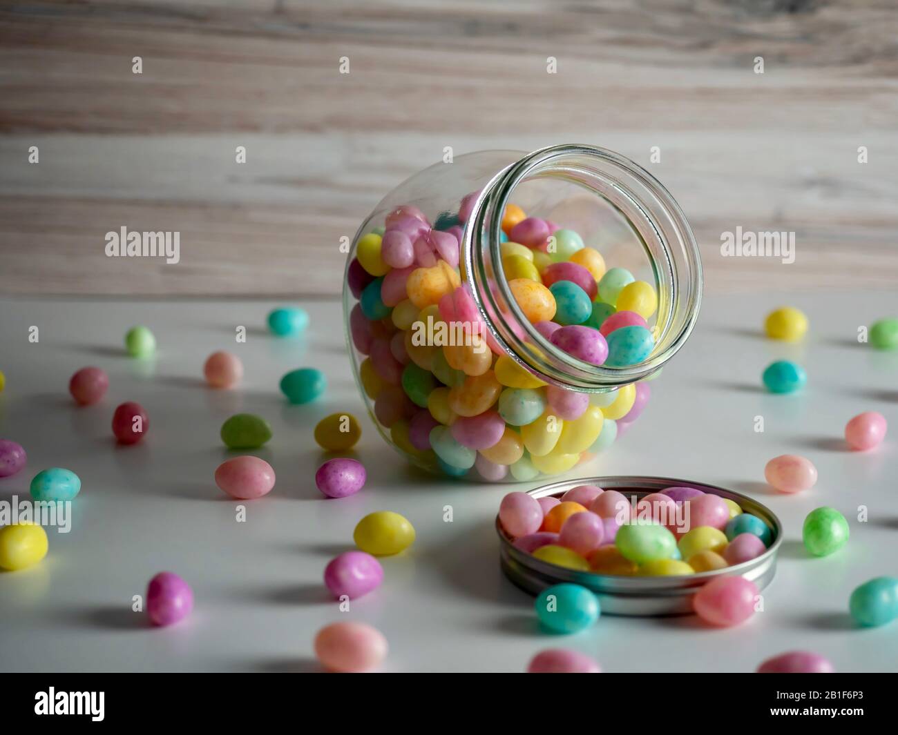 Clear glass candy jar of pastel colored Easter jelly beans spilling out ...