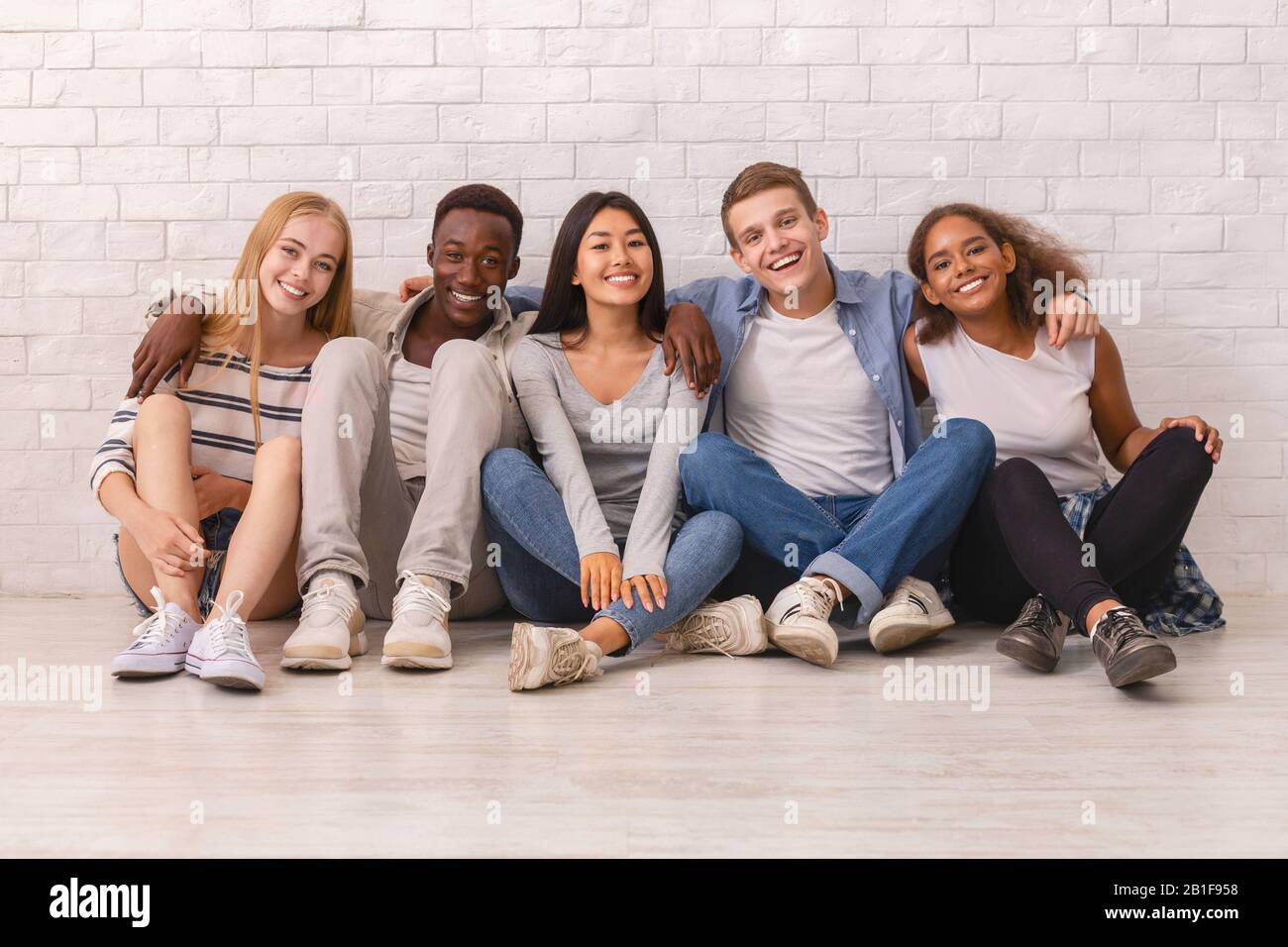 Happy students posing over white brick wall Stock Photo - Alamy