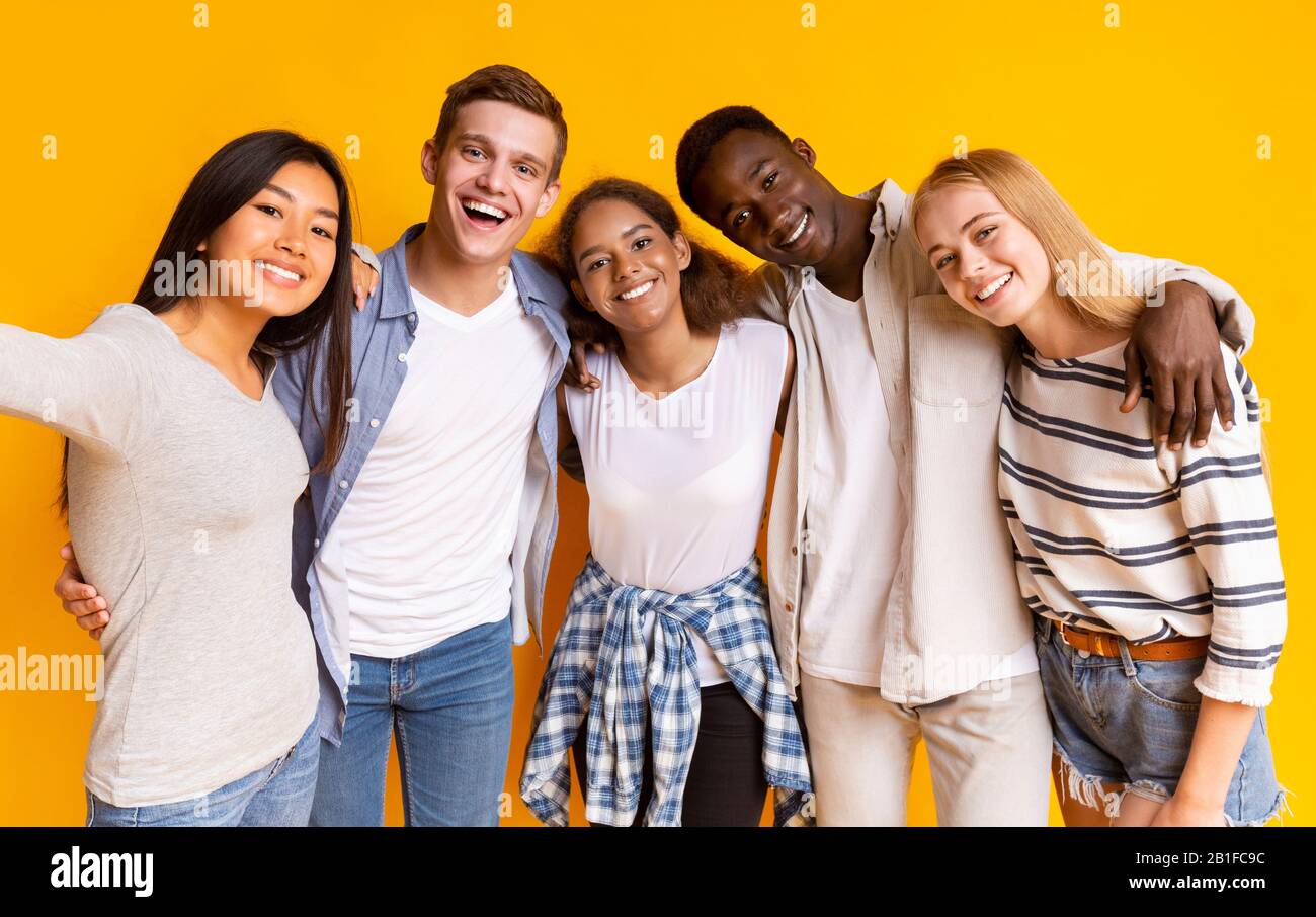 Friendly international group of teenagers taking selfie over yellow ...