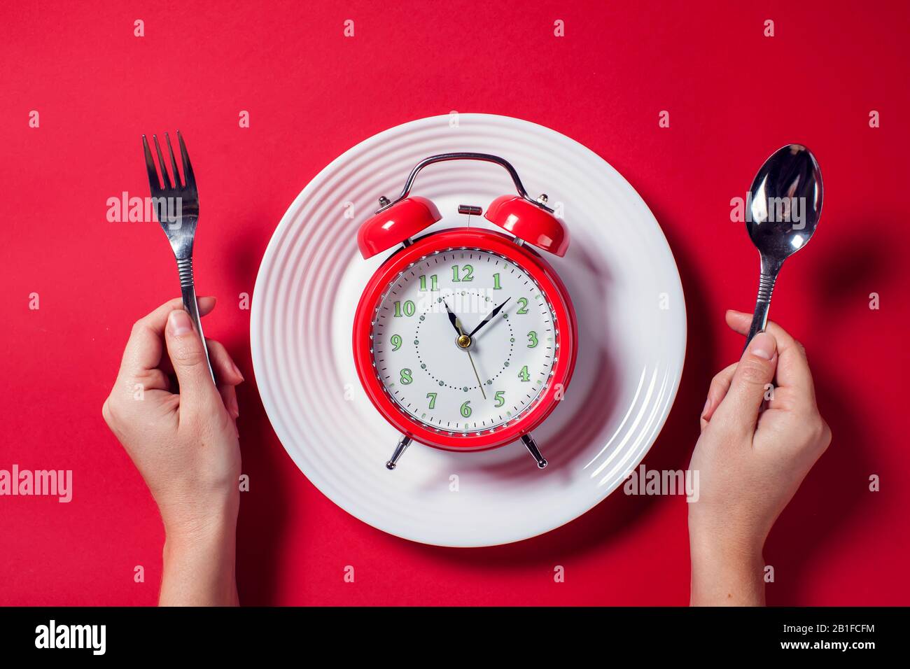 Red alarm clock on the white plate with spoon and fork on the color ...