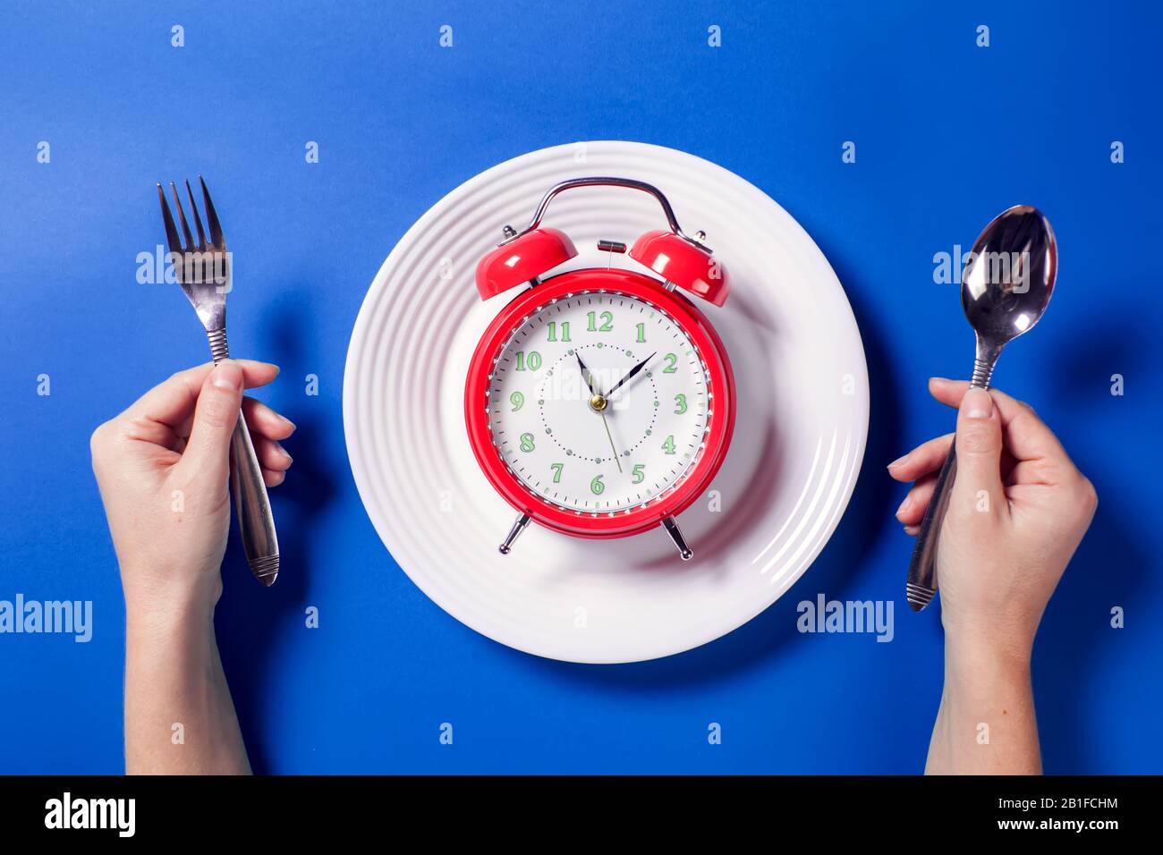Red alarm clock on the white plate with spoon and fork on the color ...