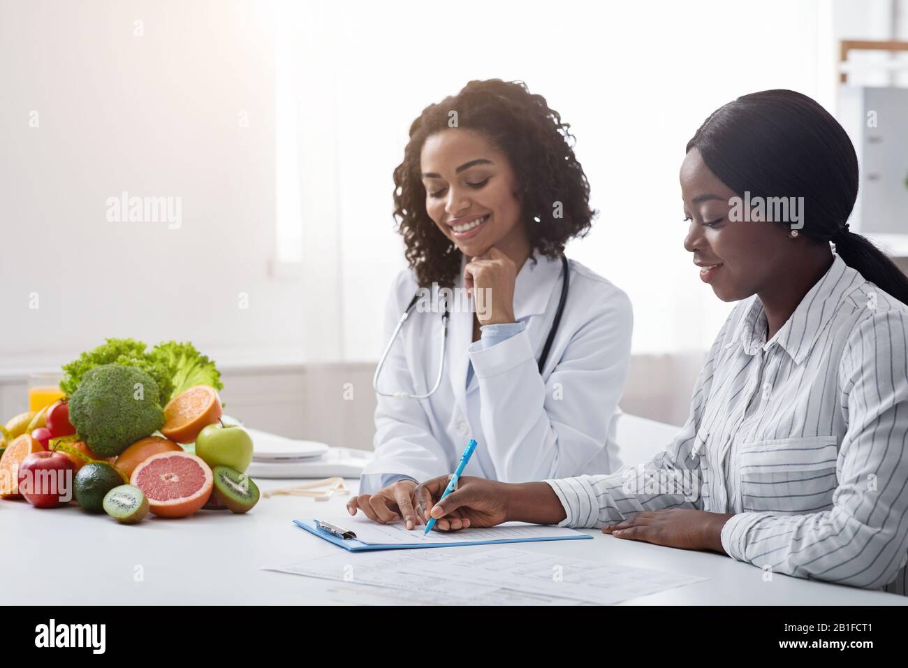 Black woman patient of nutritionist filling form during consultation ...