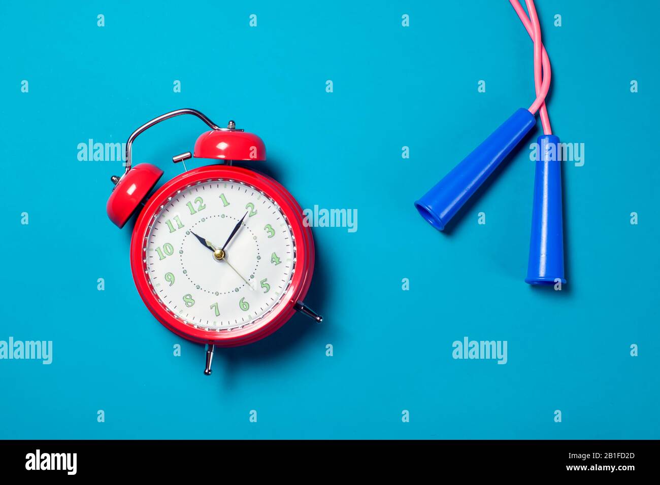Red alarm clock and jump rope on the color background. Fitness and ...