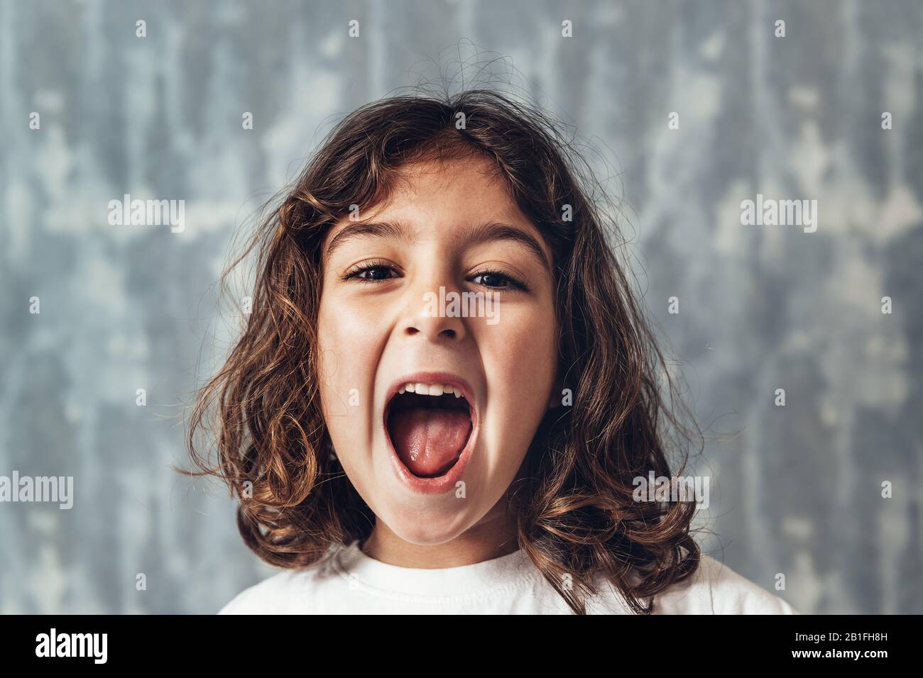 portrait of a little girl screaming out loud on a blue background ...