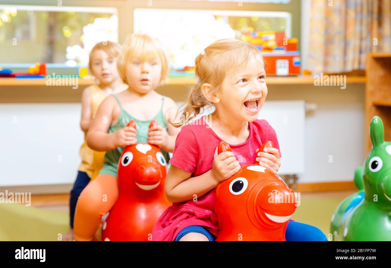 Little girls riding on play horses in kindergarten Stock Photo - Alamy