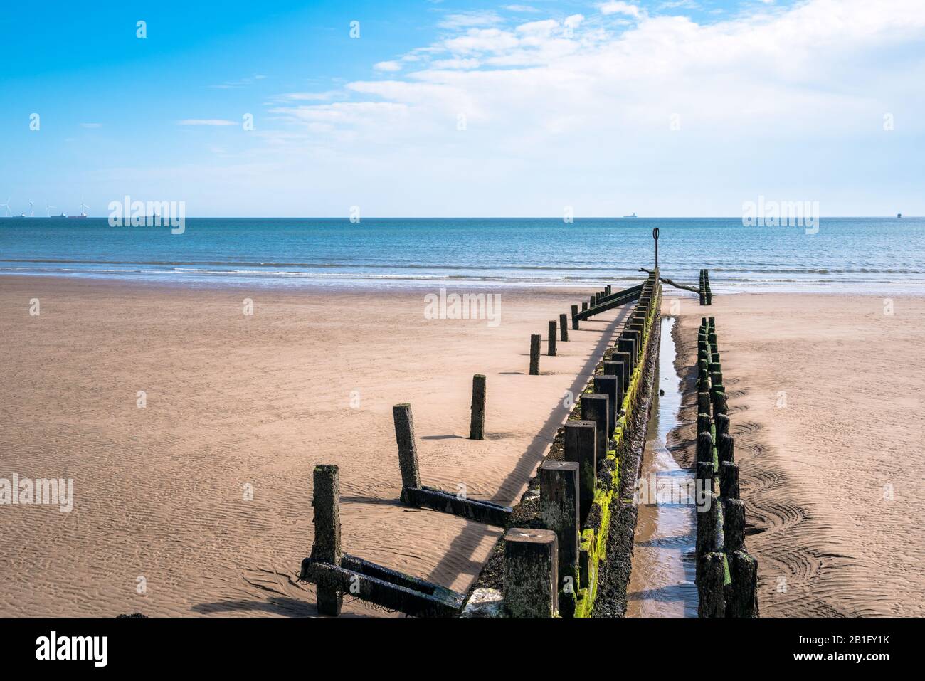 Groyne on a sandy beach on a partly cloudy spring morning. Some ships ...