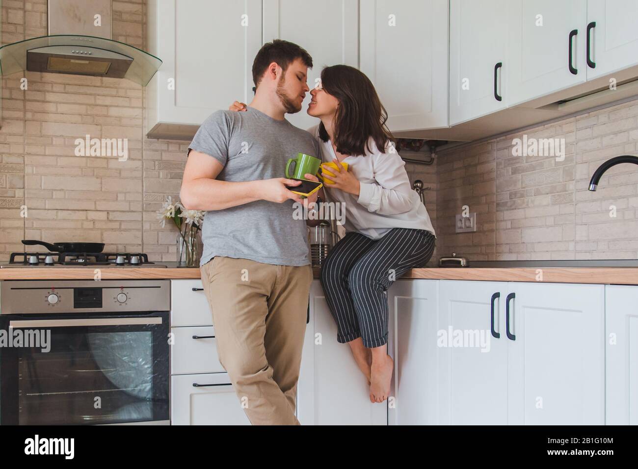 young couple kissing on kitchen while drinking tea Stock Photo - Alamy