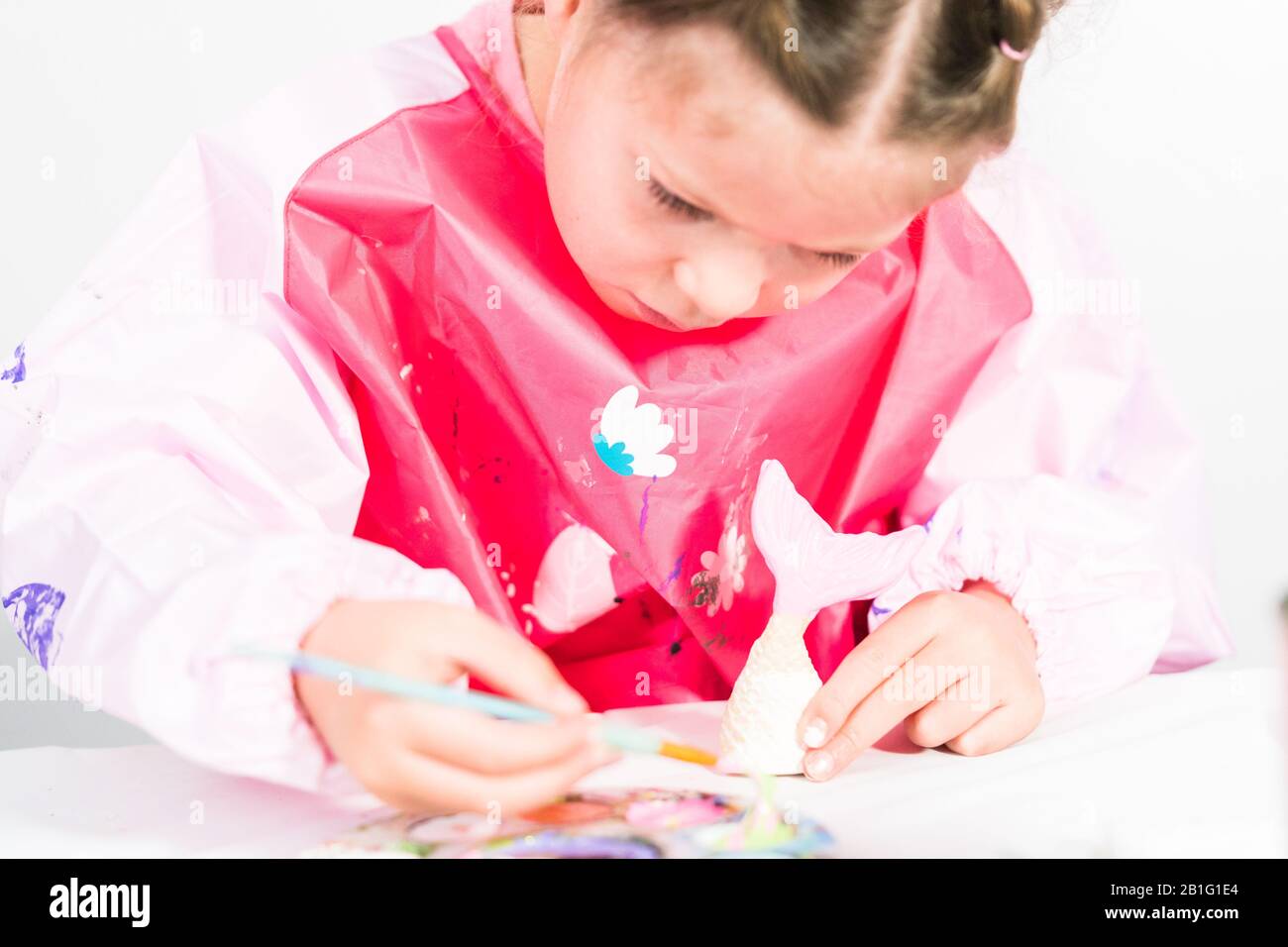Little girl painting mermaid tails made out of modeling clay with ...