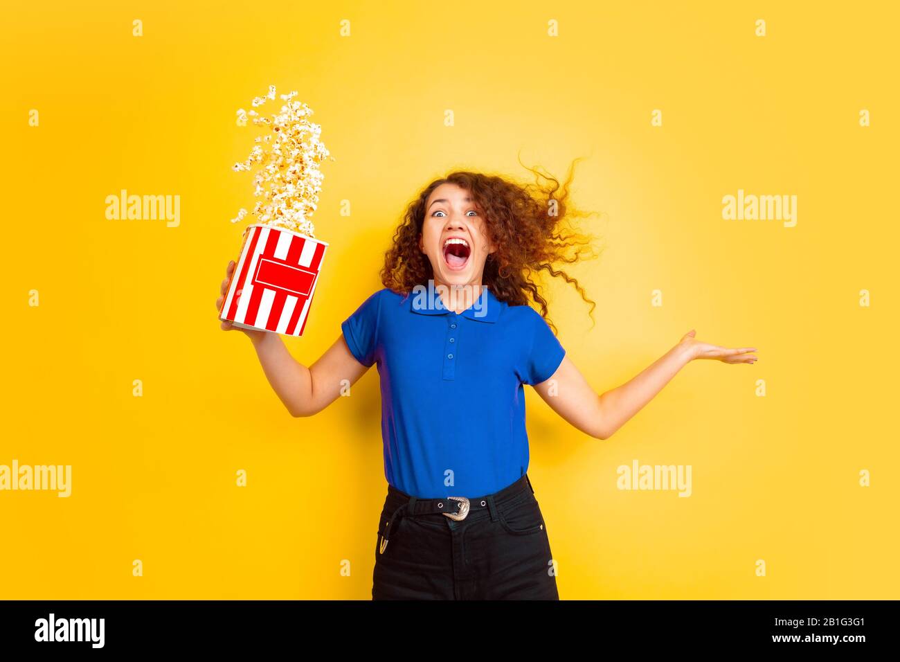 Screaming, flying popcorn. Caucasian teen's girl portrait on yellow ...