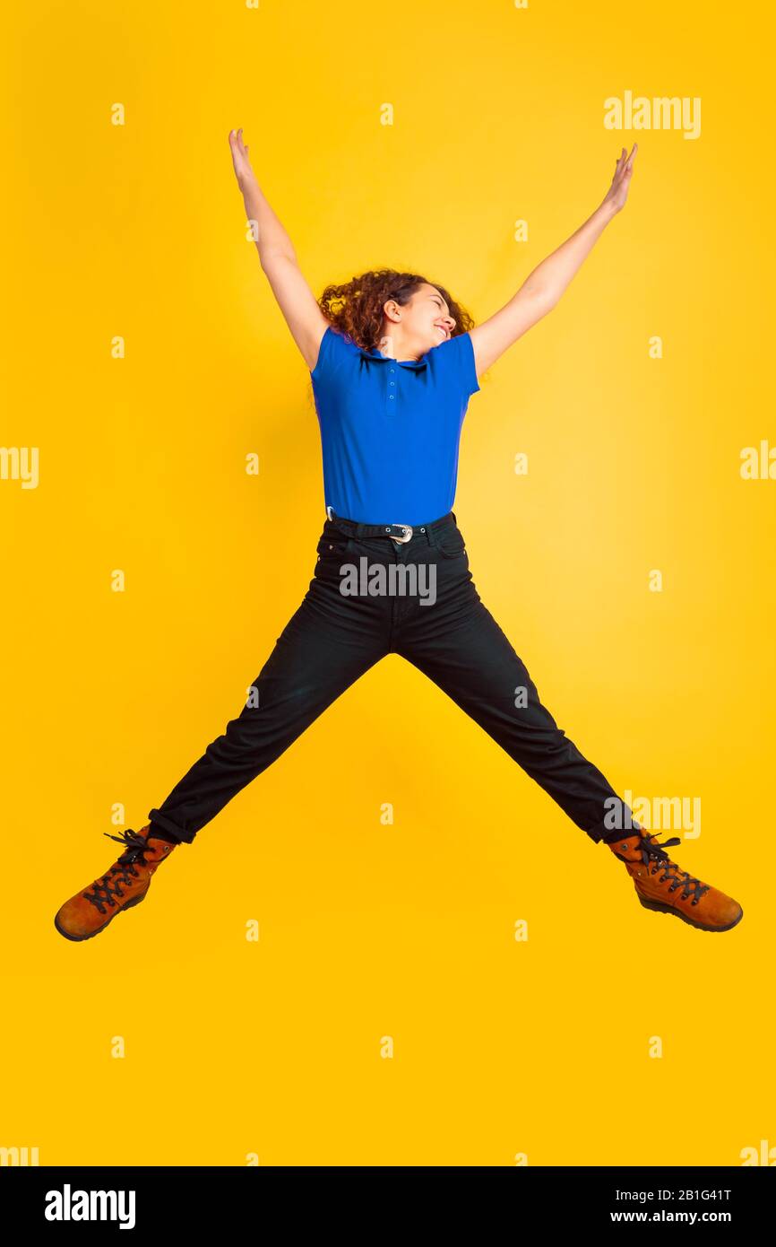 Jumping, crazy happy. Caucasian teen's girl portrait on yellow studio ...