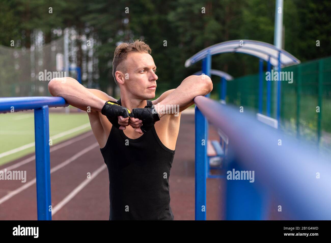 A muscular man stands leaning on parallel bars, with a bare torso. For ...