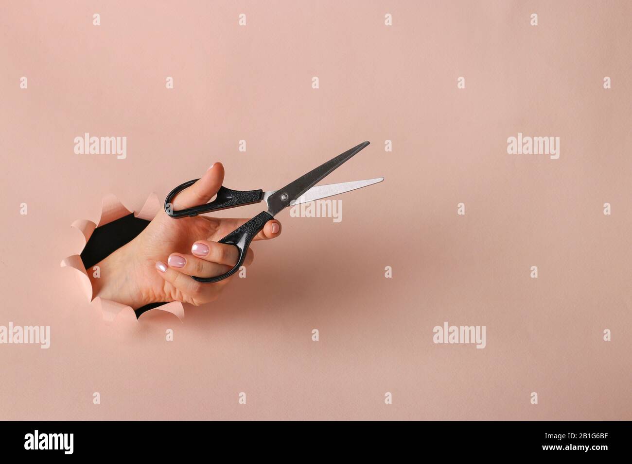 Scissors in a female hand through round hole in pink paper, Copy space ...