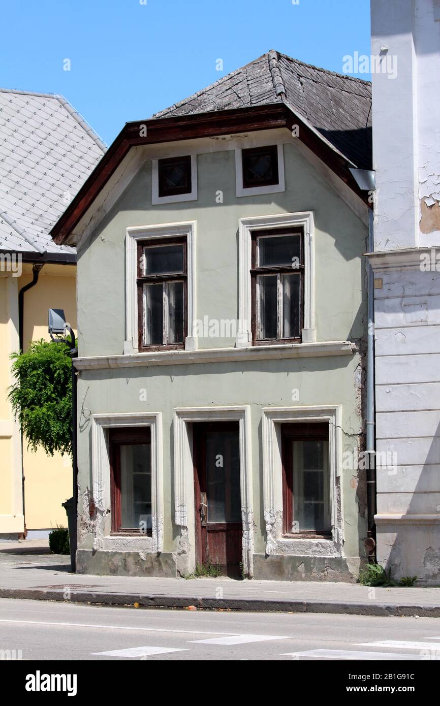 Narrow old abandoned attached suburban family house with dilapidated cracked facade and broken ...